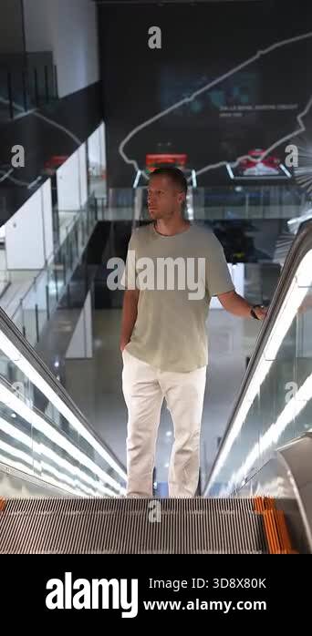 A man stands on a lit escalator in a multi level motorsport space in ...