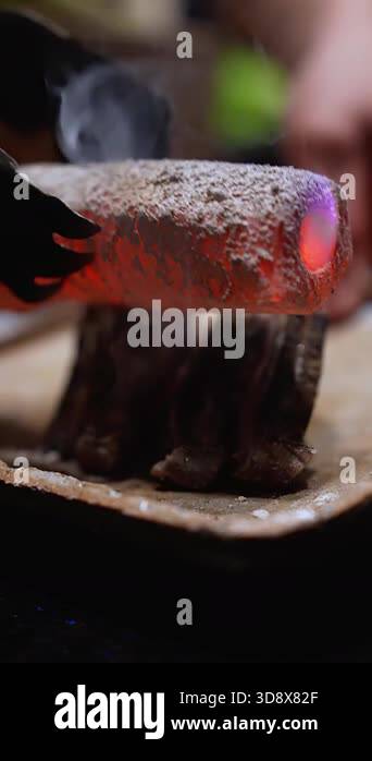 Vertical macro shows a chef pressing a white ash charcoal on fish ...