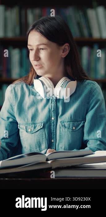 Woman learns quietly in library while listening with headphones on ...