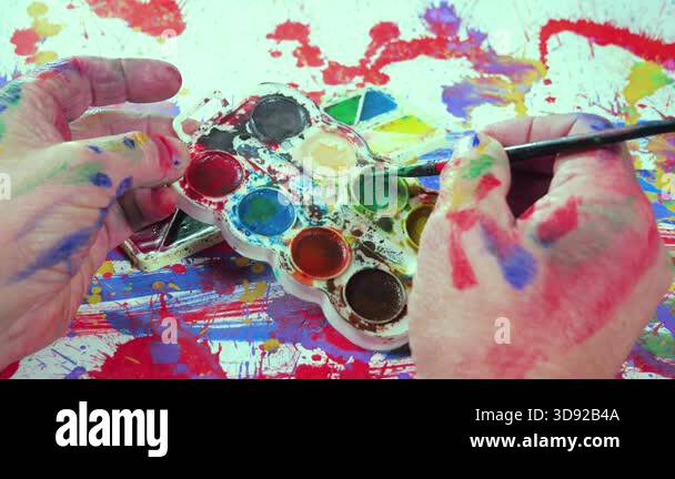 An artist applies watercolor paint to a brush. Close-up of his hands ...