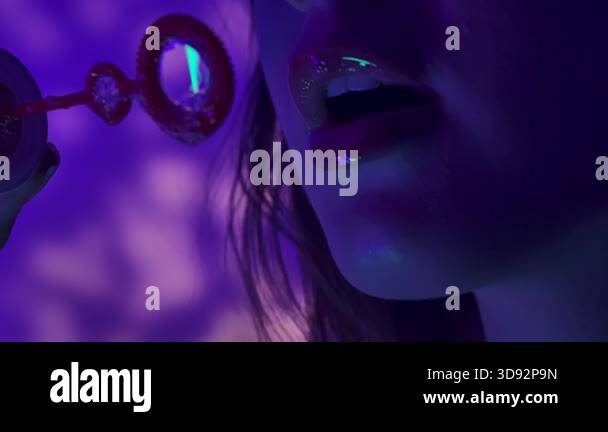 A close up of a woman blowing soap bubbles with purple and pink bokeh ...