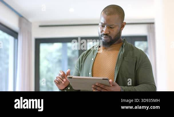 African American man tapping and swiping tablet at home gazing upward ...