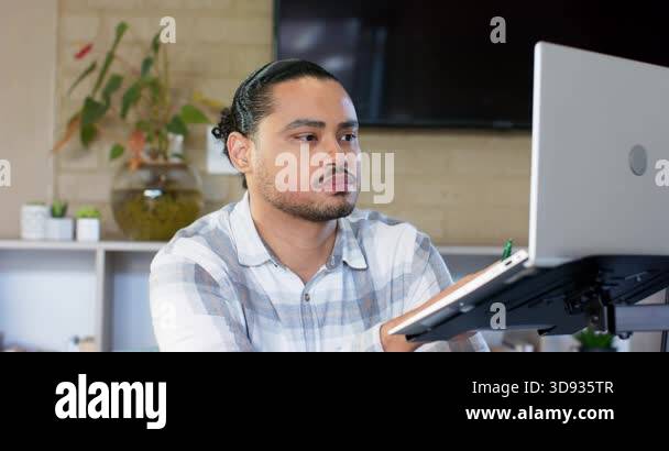 Staring at monitor at desk, man reaching for pen, pressing chin ...