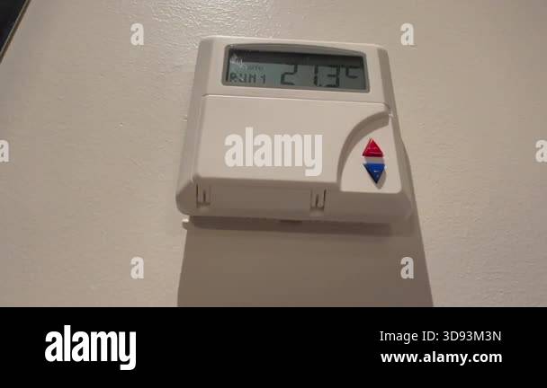 A modern digital smart thermostat mounted on a wall, displaying active ...