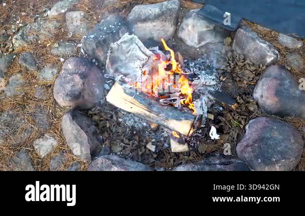 Flames flicker and crackle around logs in a stone fire pit, creating a ...