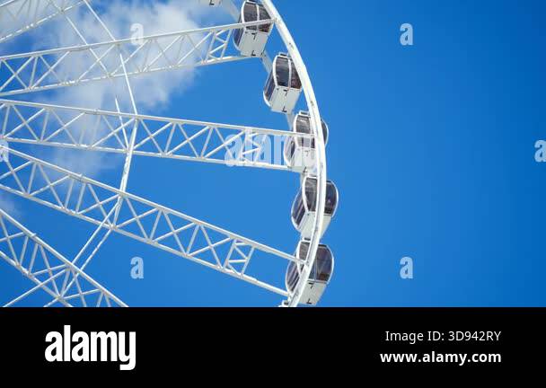 Giant white wheel rotates against bright blue sky with scattered clouds ...