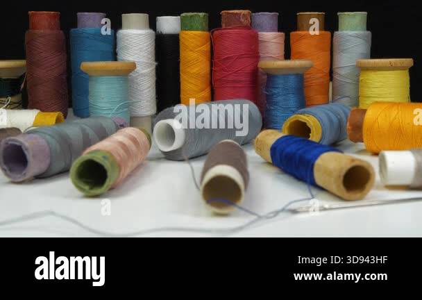 Beautiful multi-colored spools of thread lie on white table and rotates ...