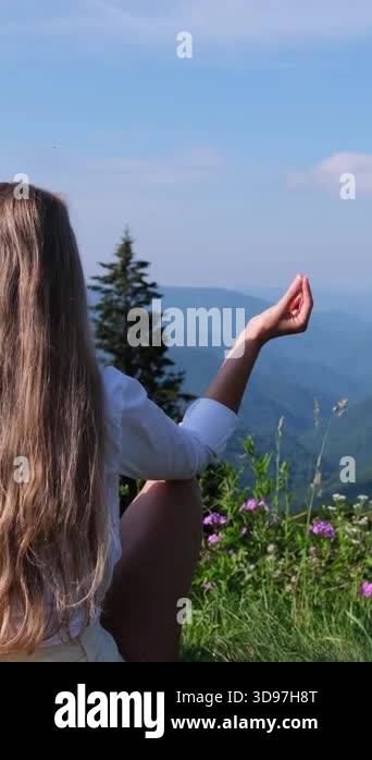 A woman sits in a calm meditation pose with one hand lifted while ...