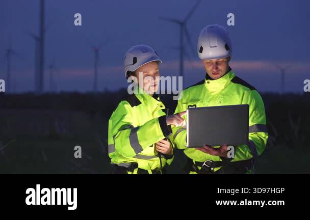 Engineers wearing safety helmets and jackets inspecting a wind turbine ...