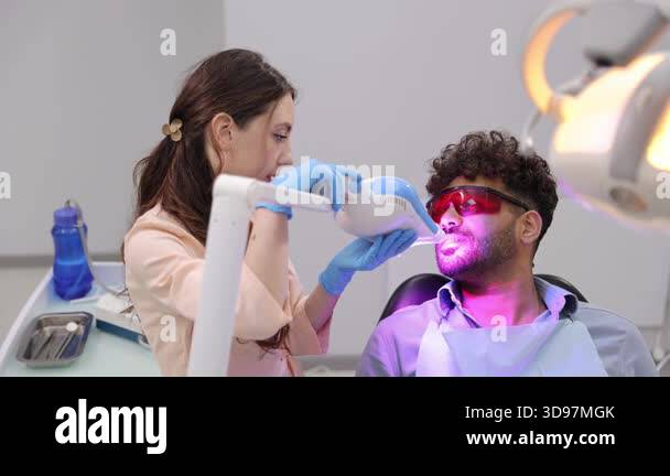 A female dentist is installing a filling under ultraviolet light for a ...