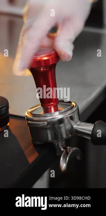 Barista tamping freshly ground coffee in metal portafilter using red ...