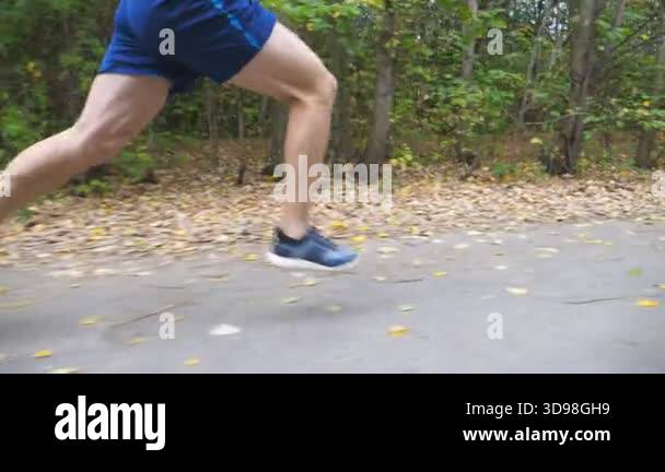 Male feet of strong athlete sprinting fast along road near forest at ...