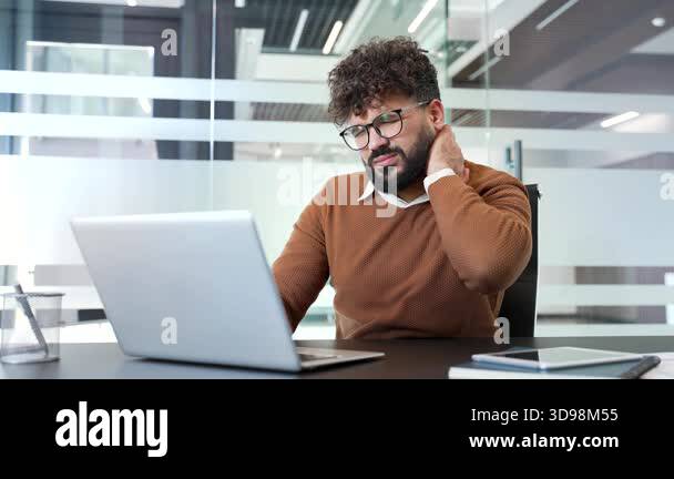 Overworked businessman suffering from neck pain while working on laptop ...