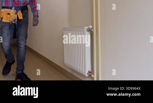 Plumber checks heating radiator valve alignment near wall pipes. Worker ...