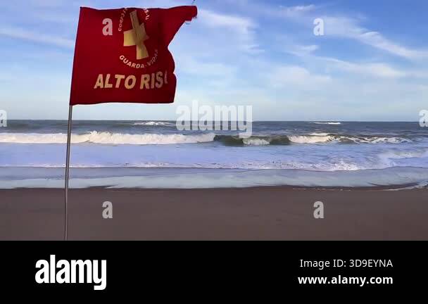 A red high risk warning flag on a beach with waves and blue sky behind ...