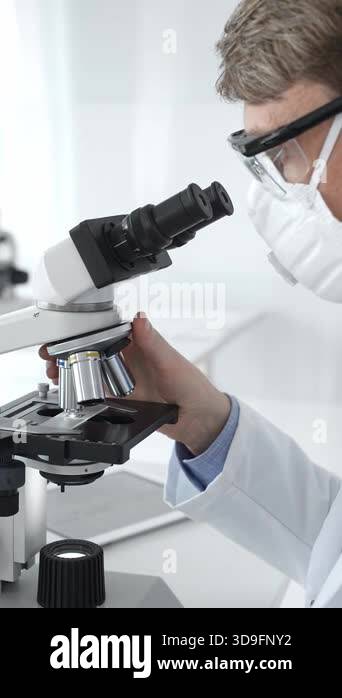 A researcher wearing a protective mask examines a sample under a ...