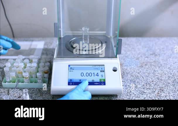 A scientist's gloved hand uses a stainless spatula to transfer a ...