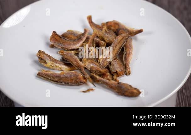 crispy fried anchovies on plate, golden pile of small fish on white ...