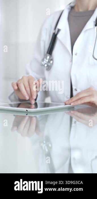 Medical professional in white coat with stethoscope using a tablet for ...