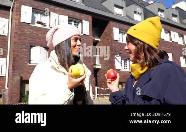 Two young smiling female friends wearing winter clothes are eating ...
