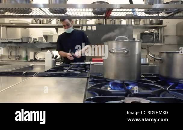 Dolly shot of a cook working in an industrial kitchen while large pots ...