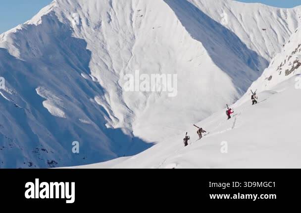 Aerial footage of four ski mountaineers carrying skis on their backs ...