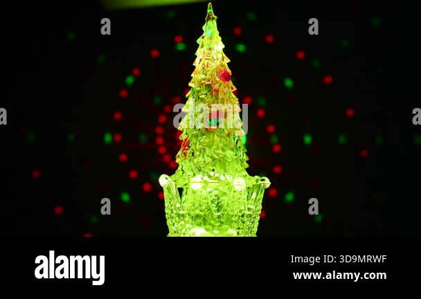 A glass Christmas tree rotates on a stand with different lighting on a ...