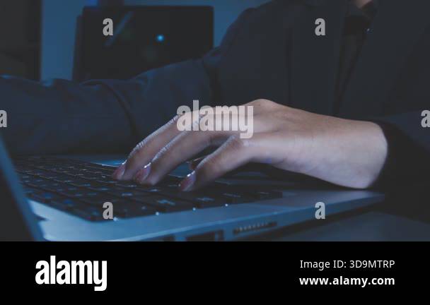 A man's hands are busy typing on a laptop keyboard during the nighttime ...