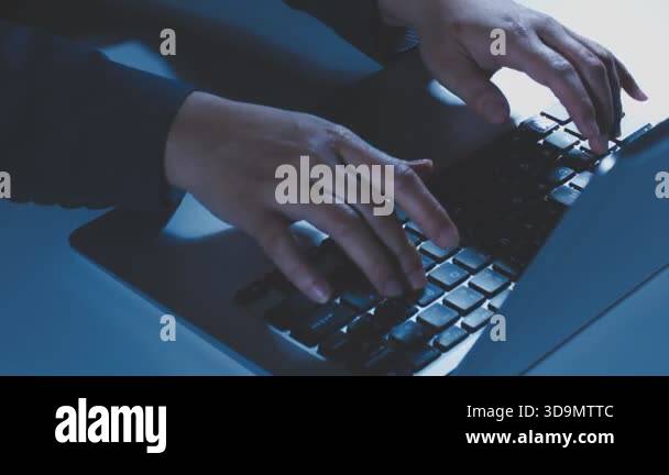 A man's hands are busy typing on a laptop keyboard during the nighttime ...