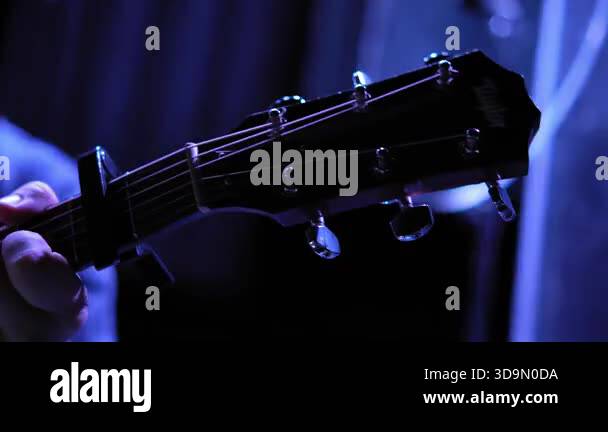 A musician plays an acoustic guitar on stage under flickering ...