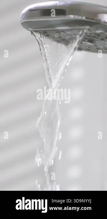 Clear water streams from a sleek shower head, illuminated by natural ...