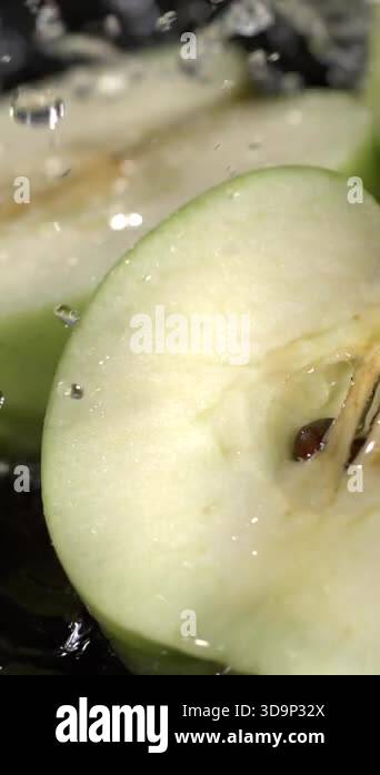 Green apples are sliced in half and drop into water, creating splashes ...