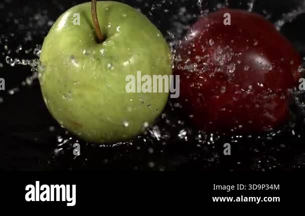 Two apples, one green and one red, drop into water creating splashes ...
