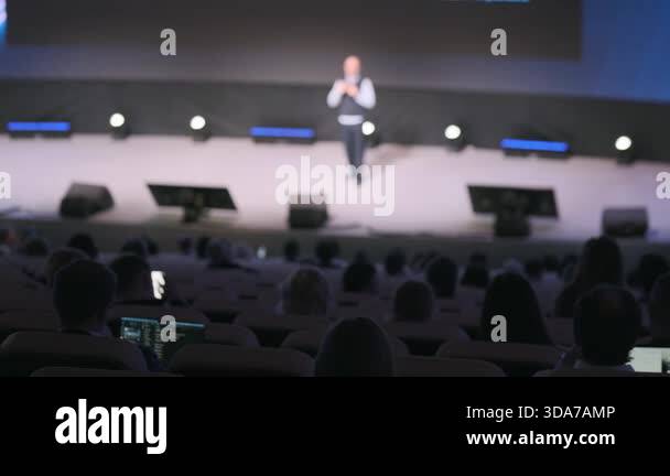 Blurred view of speaker presenting on stage at conference in auditorium ...