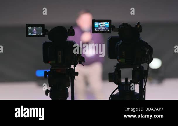 Cameras on tripods film blurred speaker on stage during interview and ...