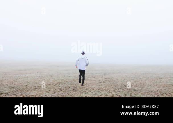 Man, runner in leggings and hoodie is running on meadow in frosty, fog ...
