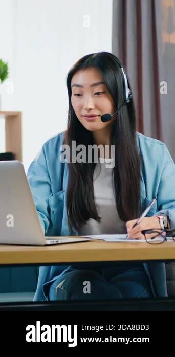 Beautiful smiling calm skilled young asian girl in headset sitting in ...