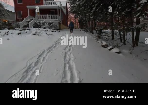 young man walking up the driveway covered with snow at sunset in ...