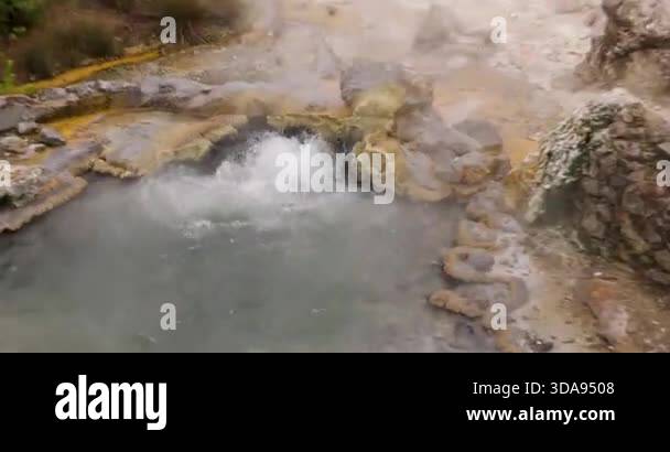 A large bubbling volcanic hot spring pond splashing water and steam at ...