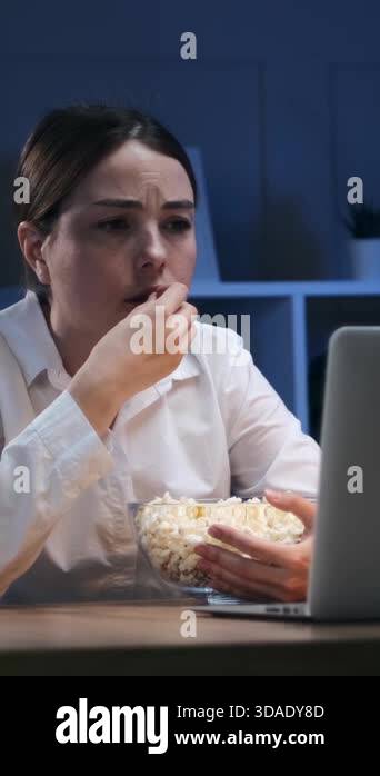 Sad young businesswoman eating popcorn and watching sad movie on laptop ...