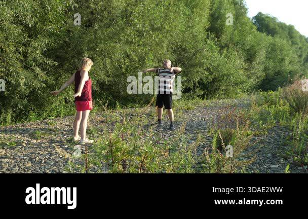 Two people perform morning physical exercises on a rocky riverside ...