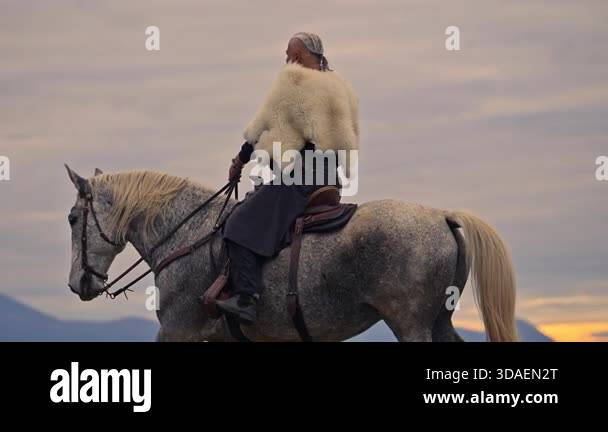 Elderly Viking warrior in fur cloak riding gray horse across open field ...