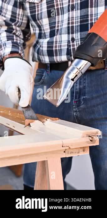 Carpenter using heat gun and wood scraper removes paint from old wooden ...