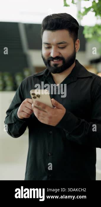 Portrait of Indian man office employee smiles and uses smartphone in ...