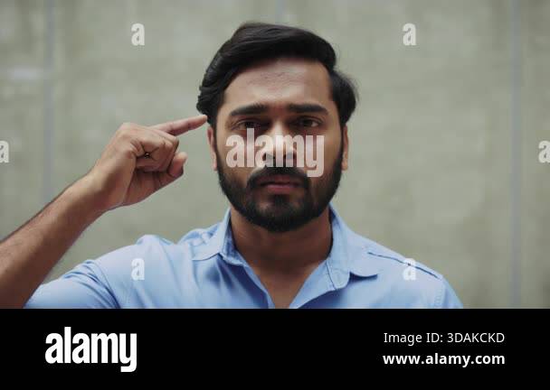 Portrait of young Indian man twists finger near head standing on grey ...