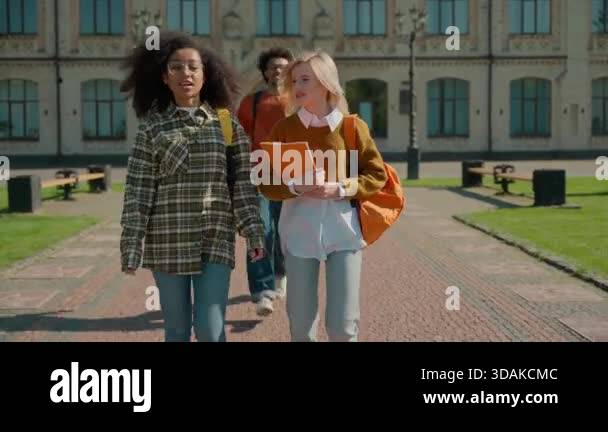 Two multiracial female students walking talking African American guy ...