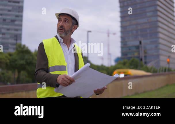 Middle aged architect wearing a hard hat and safety vest analyzing ...