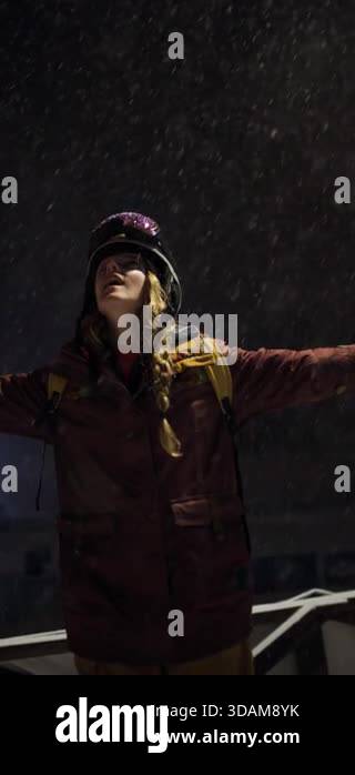 Young woman with outstretched arms enjoys the snowfall at night. She is ...