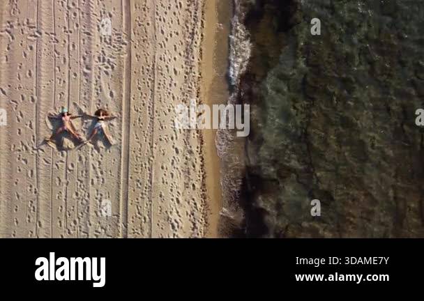 Two girls make sand angels on a beautiful beach next to the ocean ...