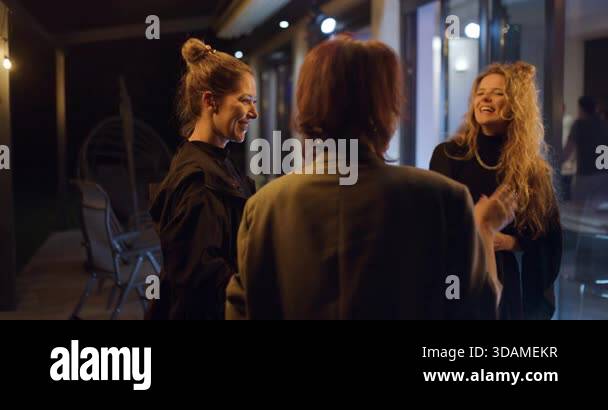 Three female friends enjoy a night out, chatting and laughing together ...